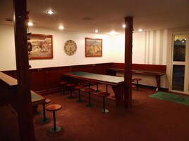 Um quarto com mesa de bilhar, banquetas de bar e um relógio na parede.