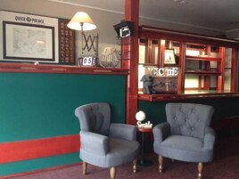 Quarto com duas poltronas cinzentas, uma luminária, um quadro emoldurado, um sinal de boas-vindas e uma estante com objetos decorativos.