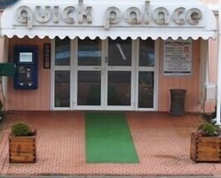 Um edifício com uma placa indicando "Quick Palace" e um tapete verde que leva à entrada.