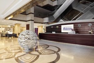 Uma área de recepção de hotel com design moderno, incluindo um balcão de atendimento, uma esfera decorativa grande e uma escada rolante.