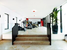 Espaço interior moderno com escada que leva a um andar superior, equipamentos de ginástica e uma grande planta em vaso.