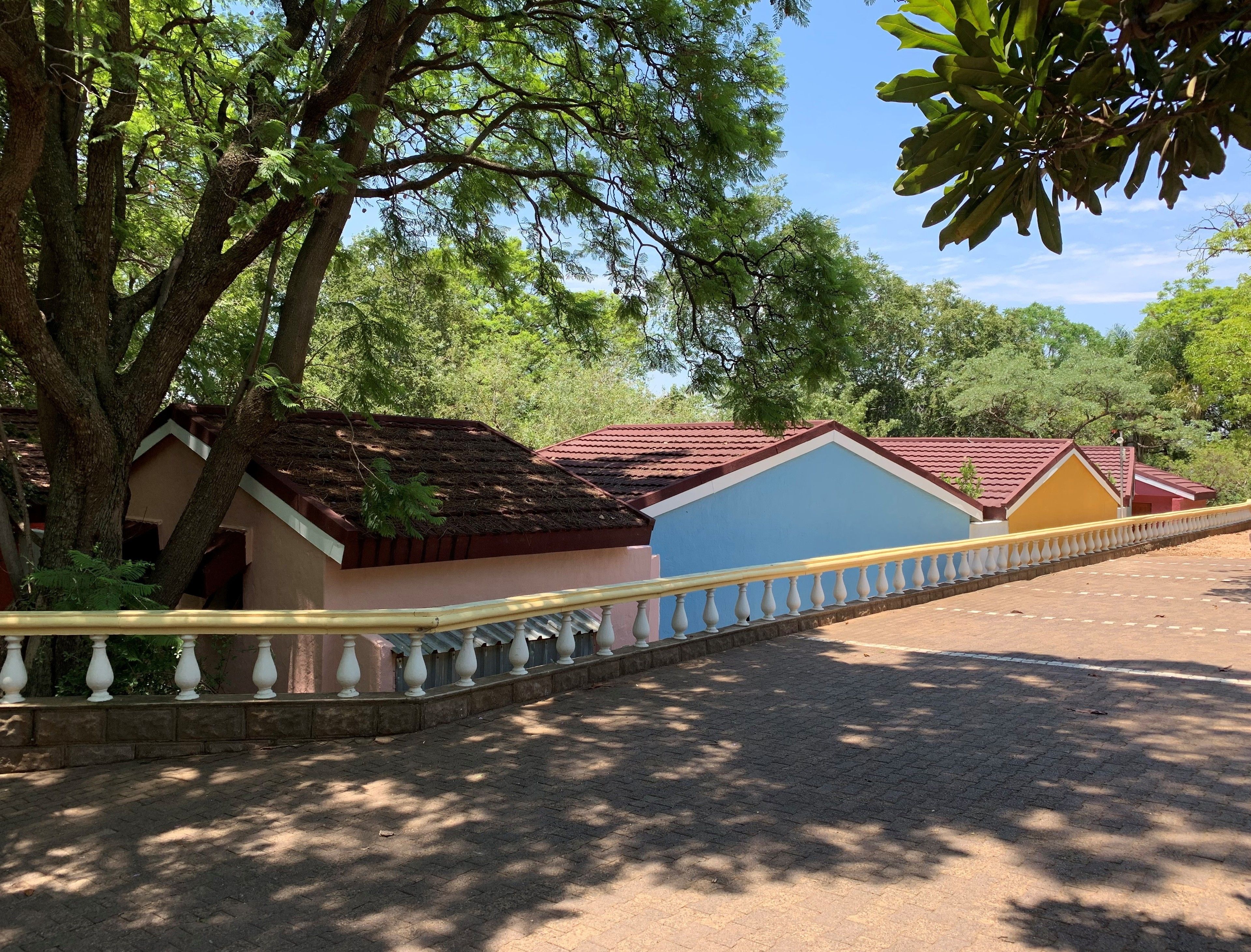 Uma fileira de pequenas casas coloridas com telhados vermelhos, cercadas por árvores e um caminho pavimentado.