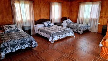 Quarto com três camas, cada uma com roupa de cama estampada, cabeceiras de madeira e chão de azulejos.