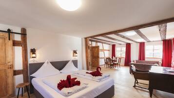 Quarto de hotel com uma cama, um banquinho de madeira, uma mesa e uma cadeira.