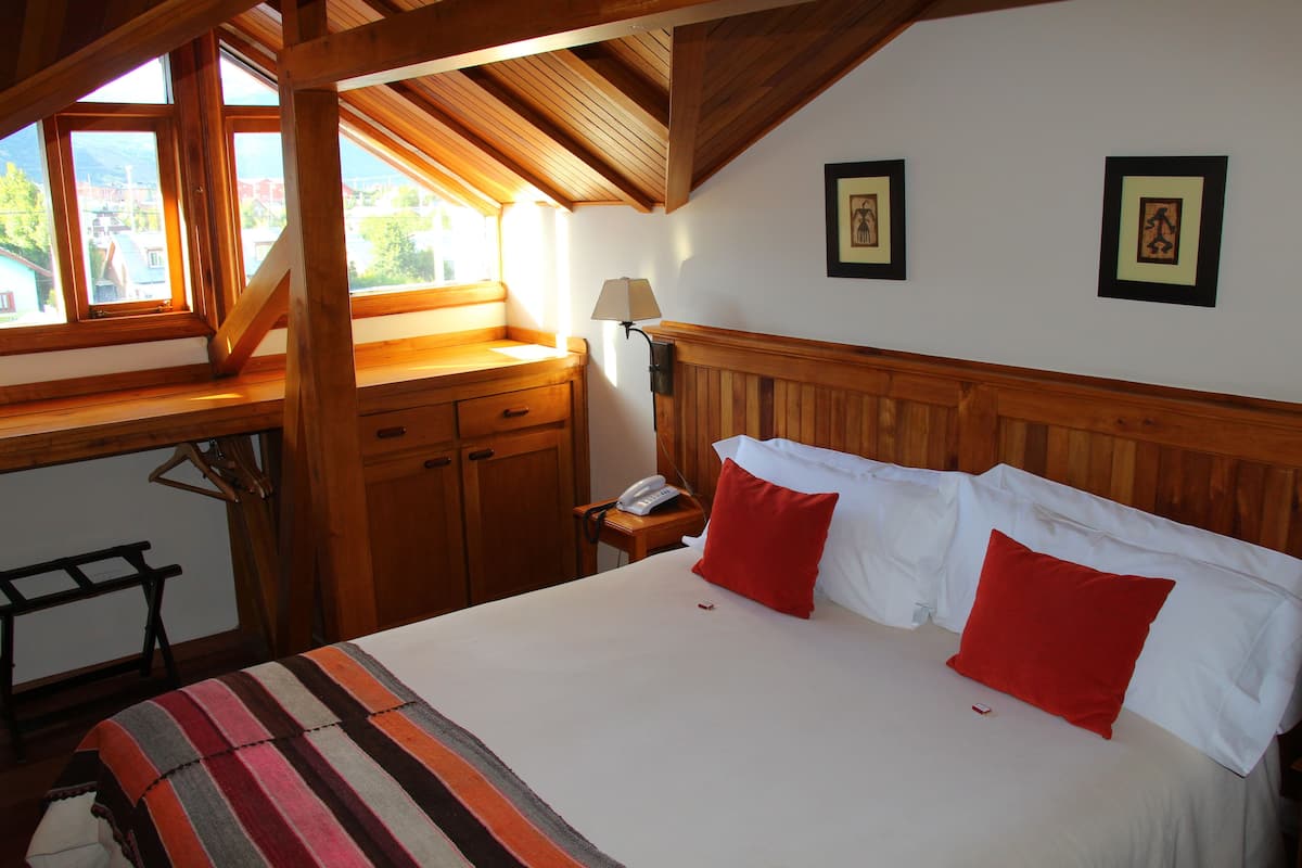 Quarto com uma cama grande, cabeceira de madeira e janela com vista para edifícios.