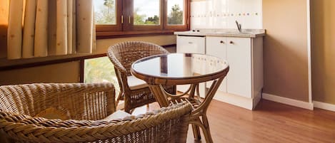 Quarto com mesa de jantar e cadeiras de vime, cozinha com armários brancos e janela com cortinas.