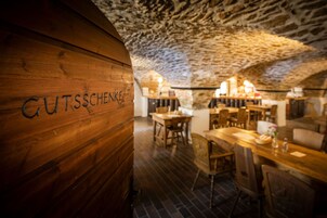 Interior de restaurante com paredes de madeira e teto de pedra. Mesas e cadeiras dispostas para refeições.