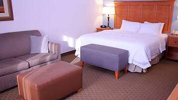 Quarto de hotel com cama, sofá, mesa de cabeceira, luminária e mala.