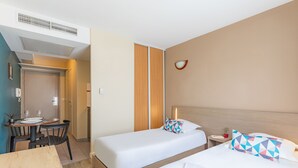 Quarto de hotel com duas camas, área de refeições e uma pequena mesa com cadeiras.