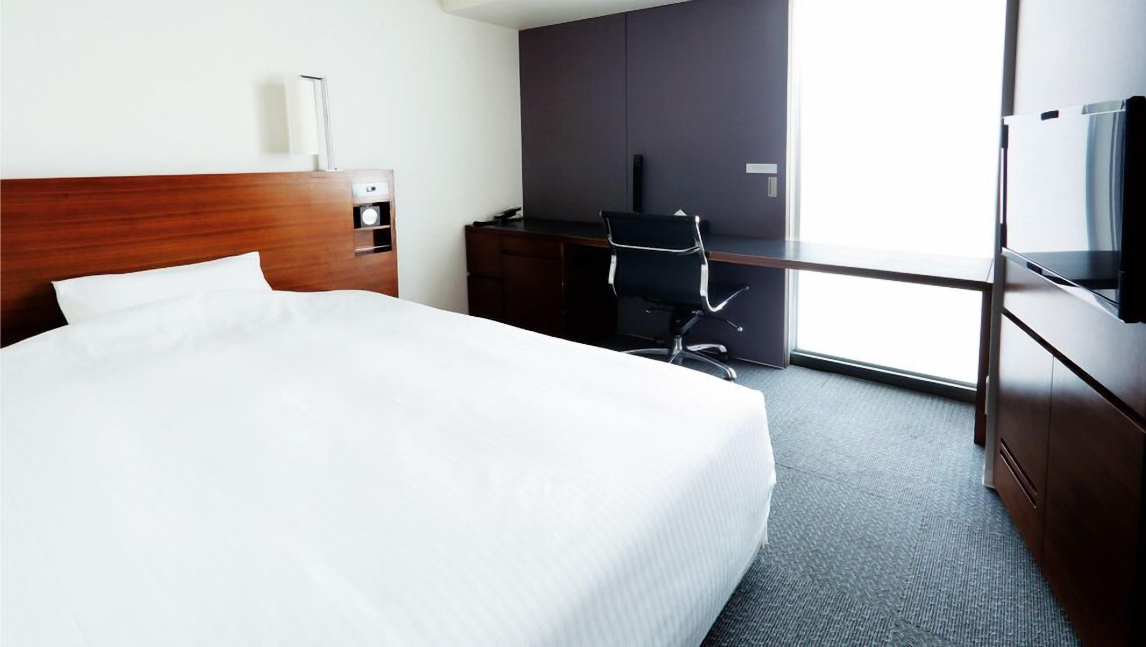 Quarto de hotel com uma cama grande, uma mesa, uma cadeira e uma televisão.