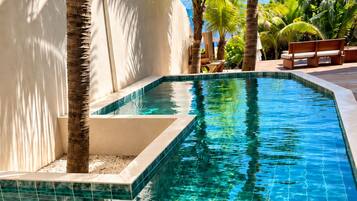 Piscina com água azul cristalina, rodeada por palmeiras e um edifício branco.