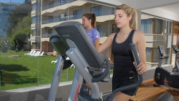Uma academia com equipamentos de ginástica e vista para um edifício com varandas.