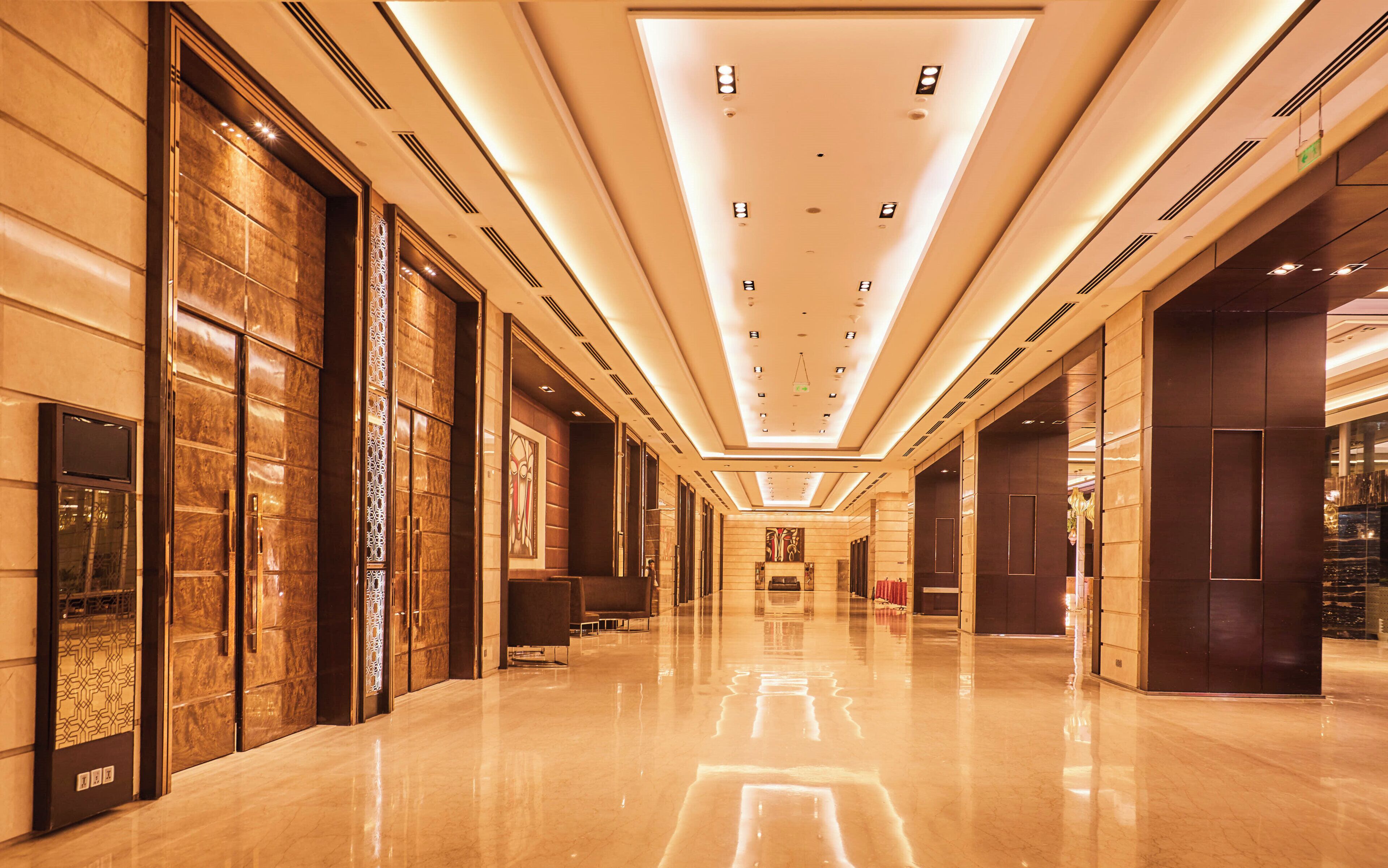 Corredor de hotel com piso lustroso, portas grandes e teto com iluminação embutida.