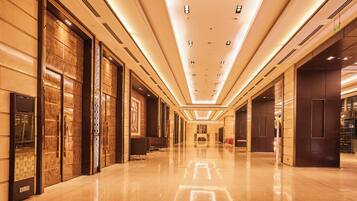 Corredor de hotel com piso lustroso, portas grandes e teto com iluminação embutida.