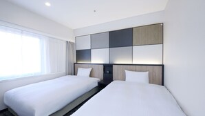 Quarto de hotel com duas camas de solteiro, uma janela grande com cortinas e uma cabeceira moderna com relógio embutido.