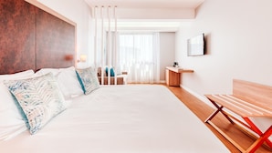 Quarto de hotel moderno com uma cama grande, uma escrivaninha de madeira e uma televisão fixada na parede.