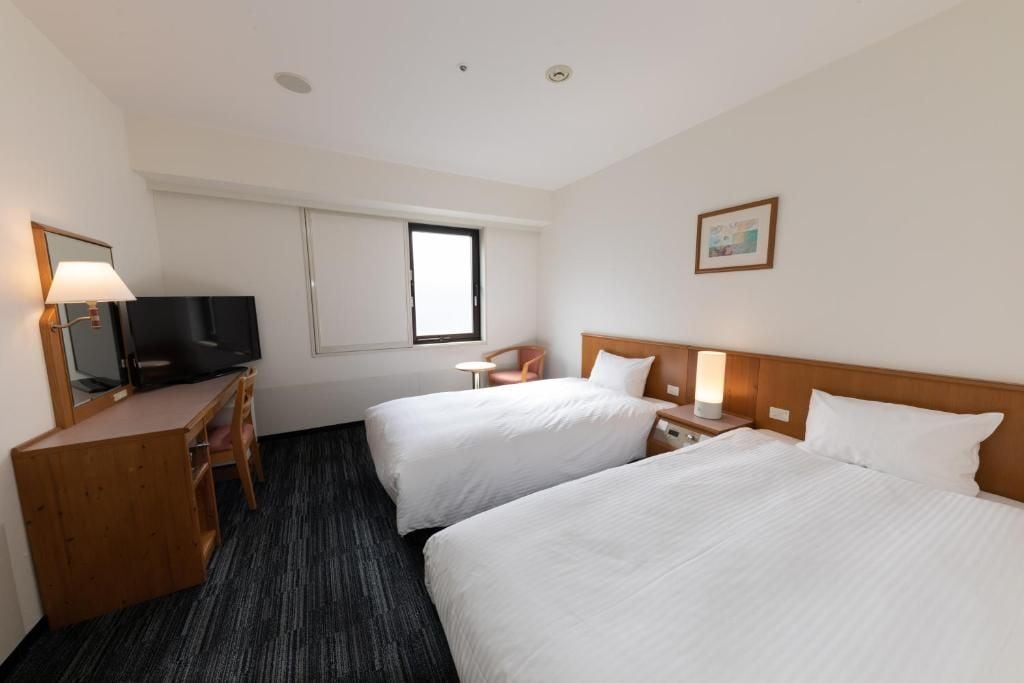 Quarto de hotel com duas camas, uma escrivaninha, televisão e uma janela.