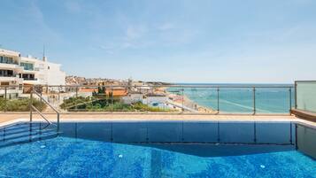 Piscina no terraço com vista para o mar e edifícios.