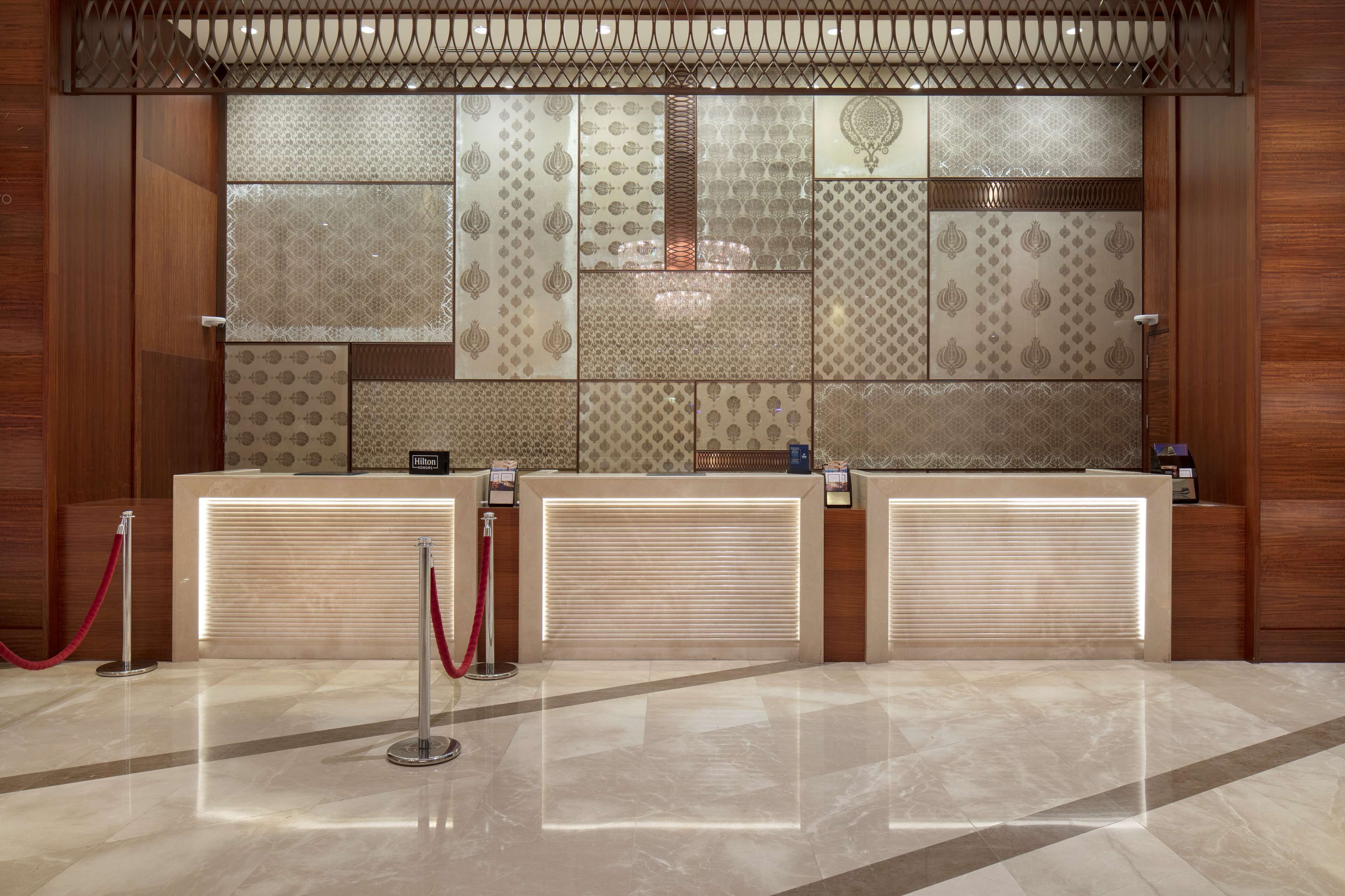 Uma área de recepção de hotel com design moderno, apresentando um painel de parede estampado, um balcão de recepção e uma corda de veludo.