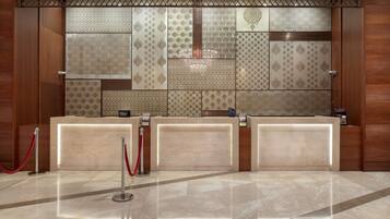 Uma área de recepção de hotel com design moderno, apresentando um painel de parede estampado, um balcão de recepção e uma corda de veludo.