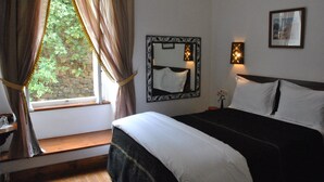 Quarto com cama, janela com cortinas, espelho e luminária na parede.