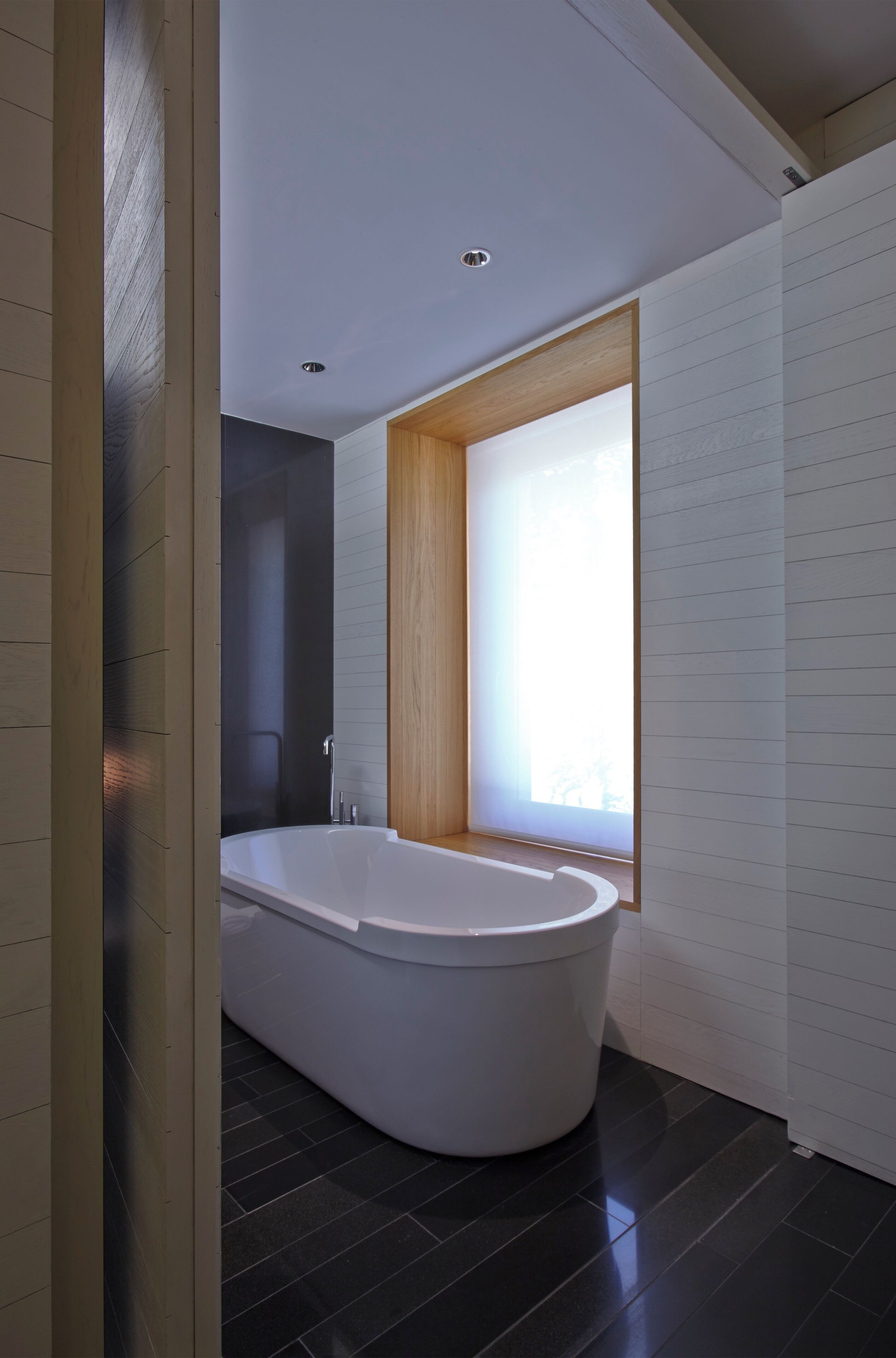 Um banheiro moderno com uma banheira de pé, uma janela com moldura de madeira e piso revestido de azulejos escuros.