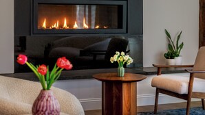 Uma sala de estar moderna com lareira, uma mesa de madeira redonda, uma cadeira e um vaso com flores.