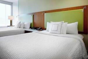 Quarto de hotel com duas camas, uma mesa de cabeceira com abajur e um telefone.