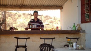 Um homem atrás do balcão, com uma bandeja de bebidas, duas cadeiras e uma mesa com um vaso de flores.