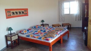 Quarto com cama de madeira, roupa de cama florida, um objeto pendurado na parede e janela com cortinas.