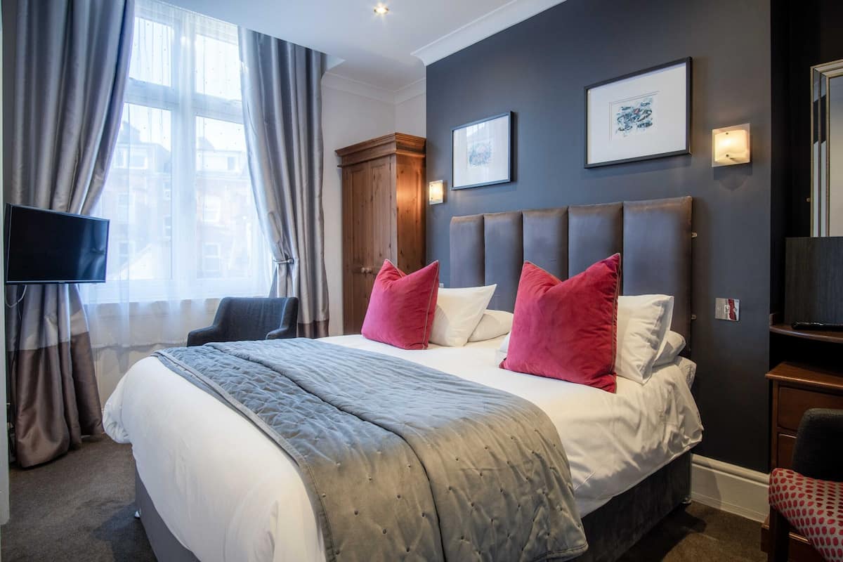 Quarto de hotel com uma cama grande, televisão, guarda-roupa e secretária com cadeira.
