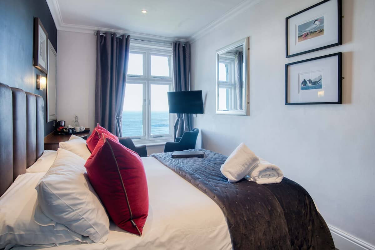 Quarto de hotel com cama, televisão, janela com cortinas e quadros nas paredes.