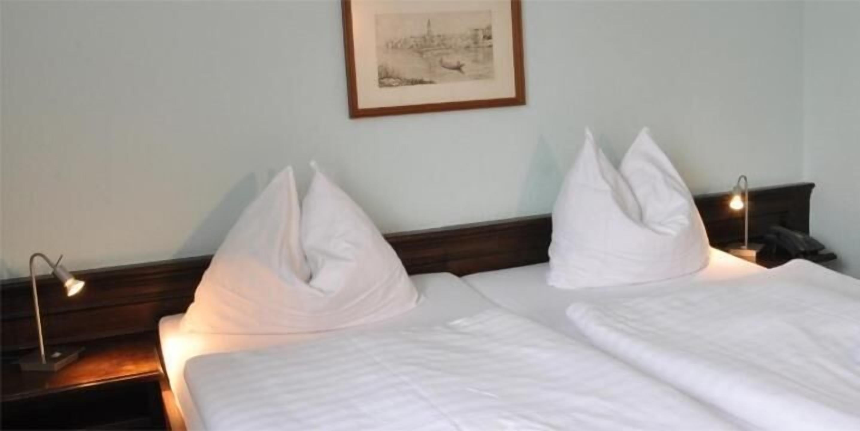 Quarto de hotel com duas camas, roupa de cama branca, um quadro na parede e abajures de cabeceira.