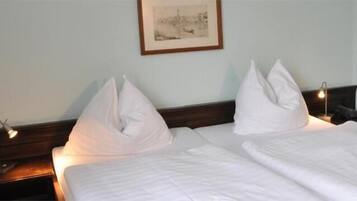 Quarto de hotel com duas camas, roupa de cama branca, um quadro na parede e abajures de cabeceira.