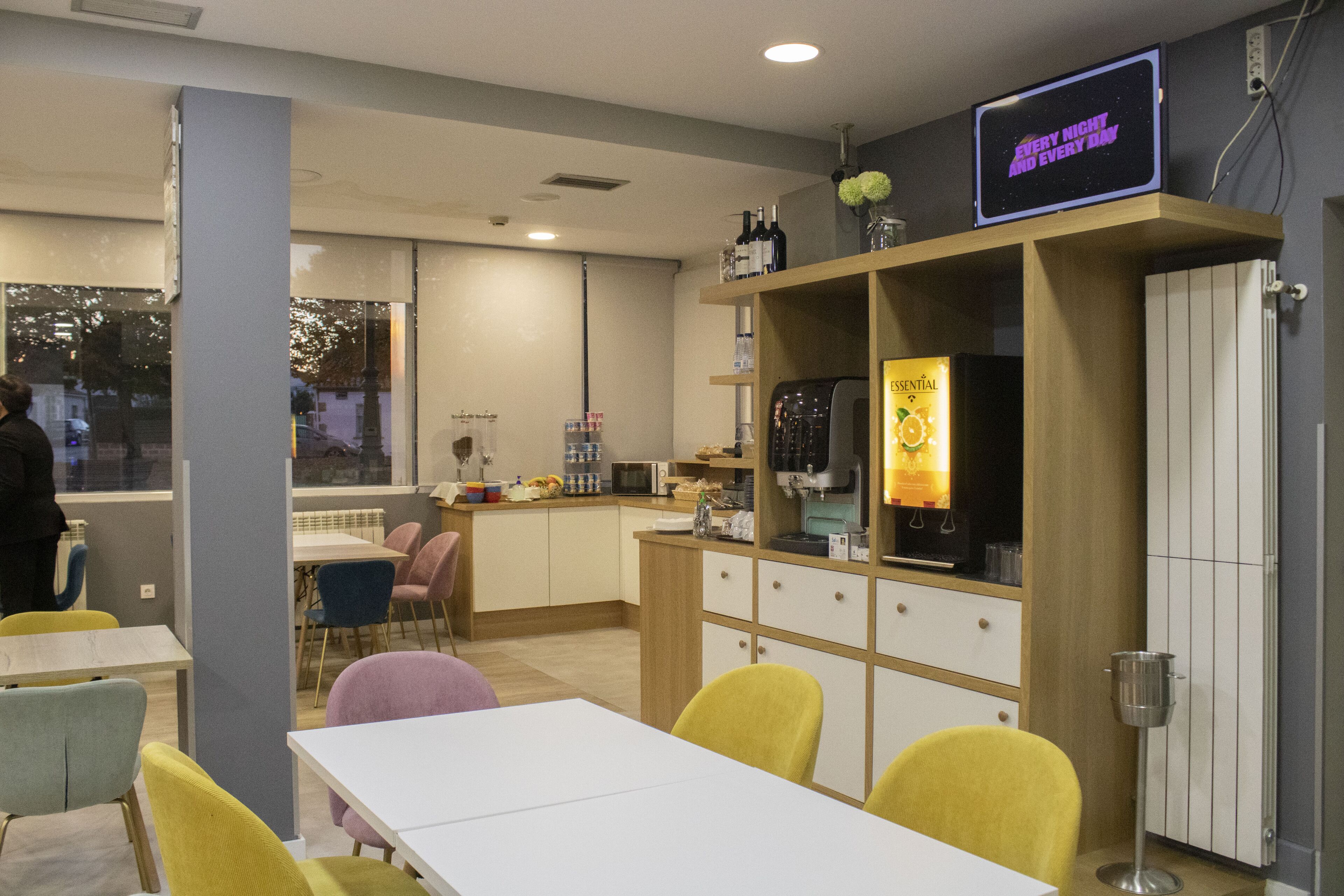 Um restaurante moderno com área de bar, cadeiras brancas e amarelas, e uma televisão exibindo 