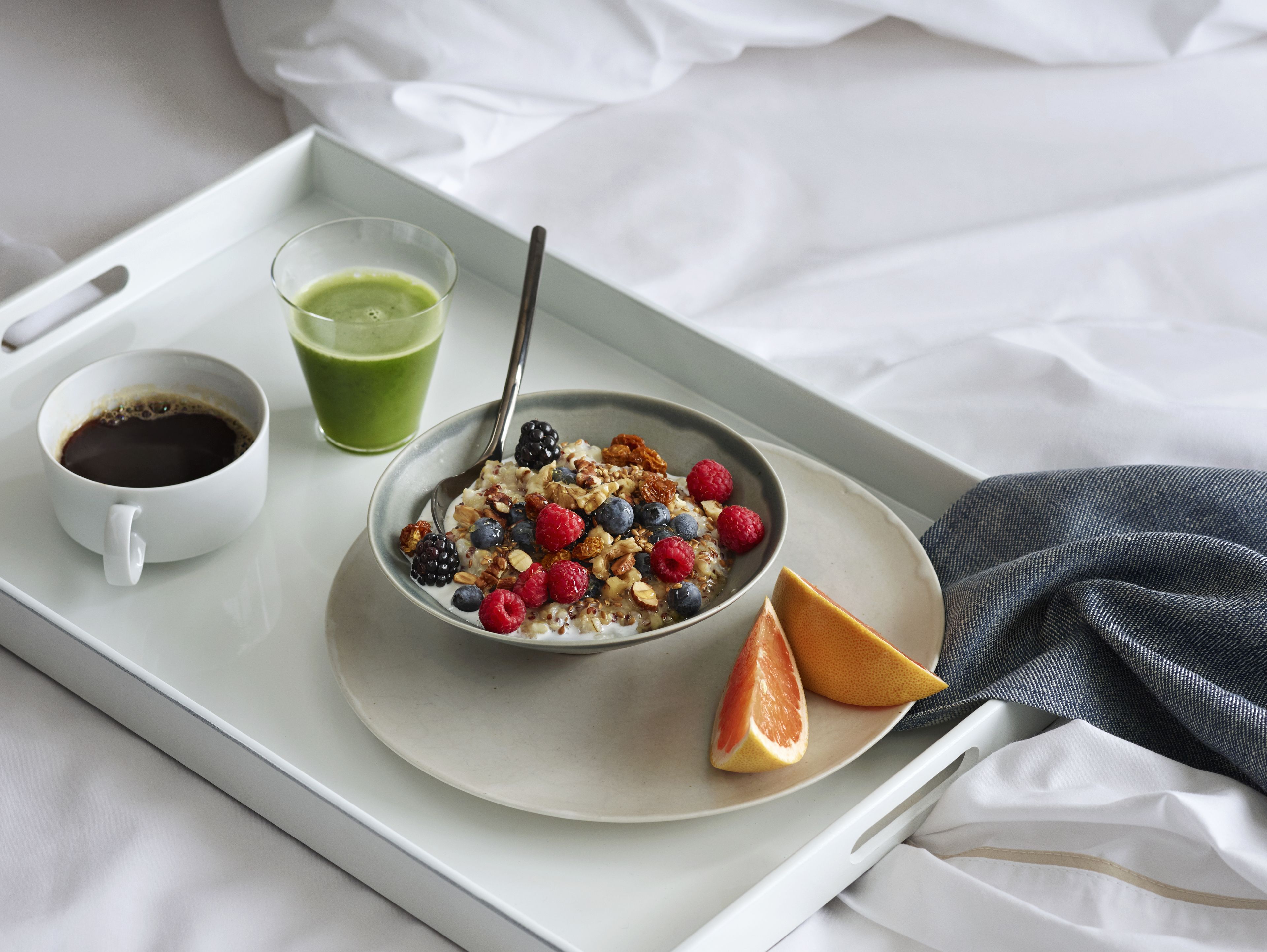 Uma bandeja de café da manhã com uma tigela de cereal coberta com frutas e nozes, uma xícara de café e um copo de suco verde.