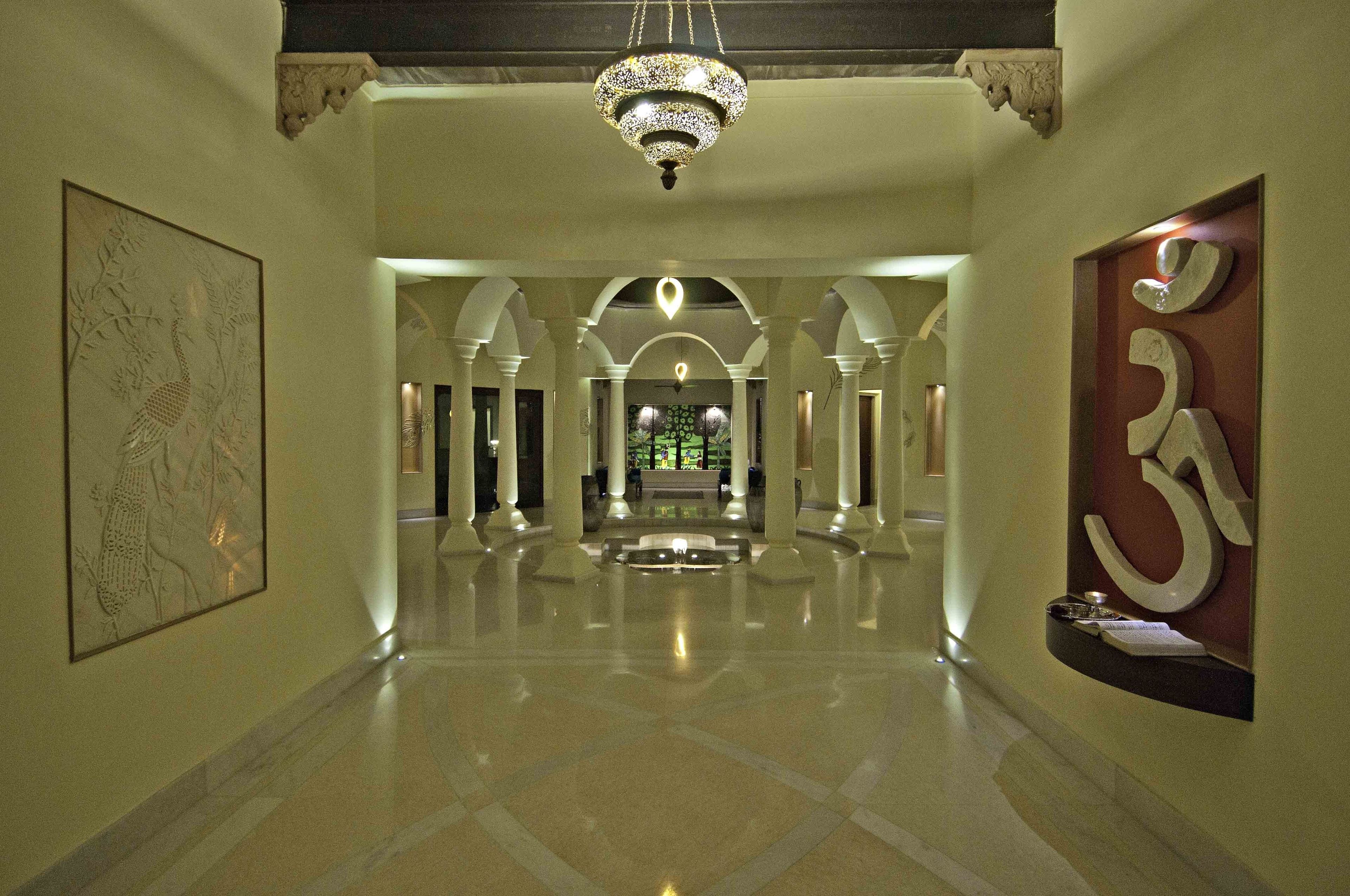 Um corredor amplo e bem iluminado, com um candelabro, uma grande obra de arte emoldurada e um detalhe decorativo na parede.