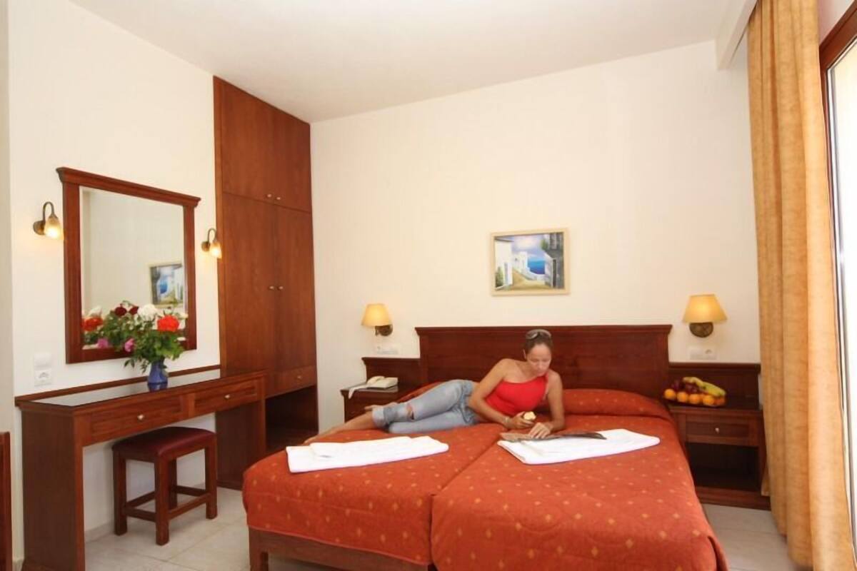 Quarto de hotel com cama, escrivaninha, cadeira, espelho e duas luminárias de cabeceira.