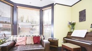 Uma sala de estar com um piano, um sofá de couro e uma janela com persianas.