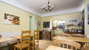 Uma sala de jantar com mesas e cadeiras de madeira, um candelabro e um cardápio em lousa na parede.