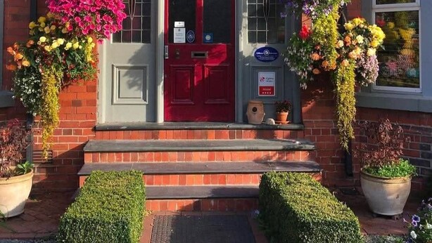 Um edifício com uma porta vermelha, degraus que levam a ele e cestos de flores de ambos os lados.