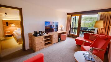 Quarto de hotel com televisão, sofá, cadeira vermelha, mesa pequena e janela com vista.