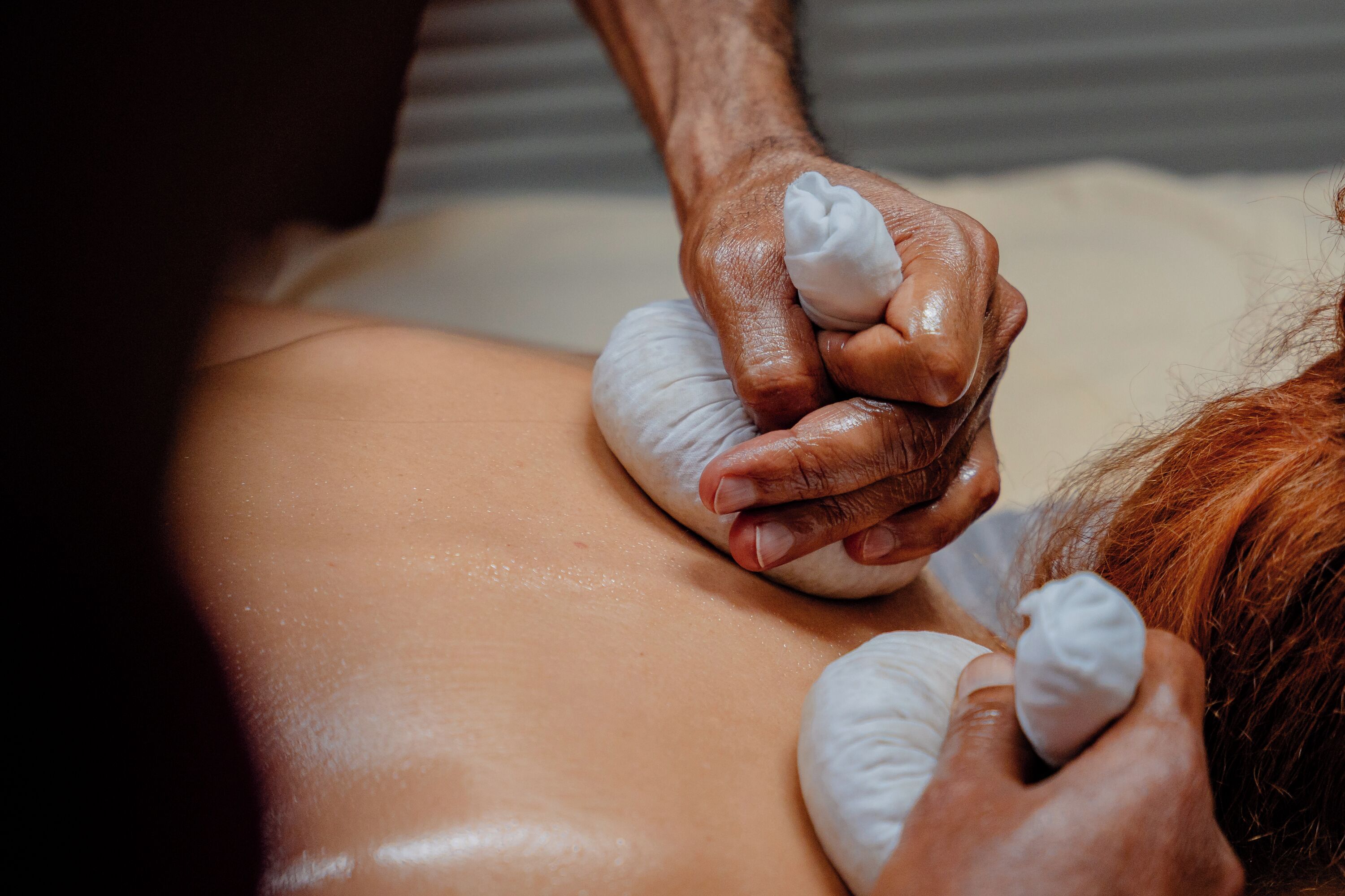 Primeiro plano de uma massagem, com mãos aplicando creme nas costas de uma pessoa.