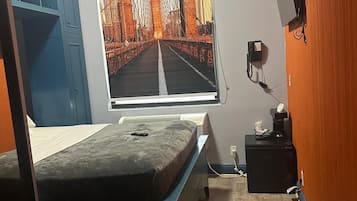 Quarto com cama, escrivaninha, cadeira, televisão e janela com vista para uma ponte.