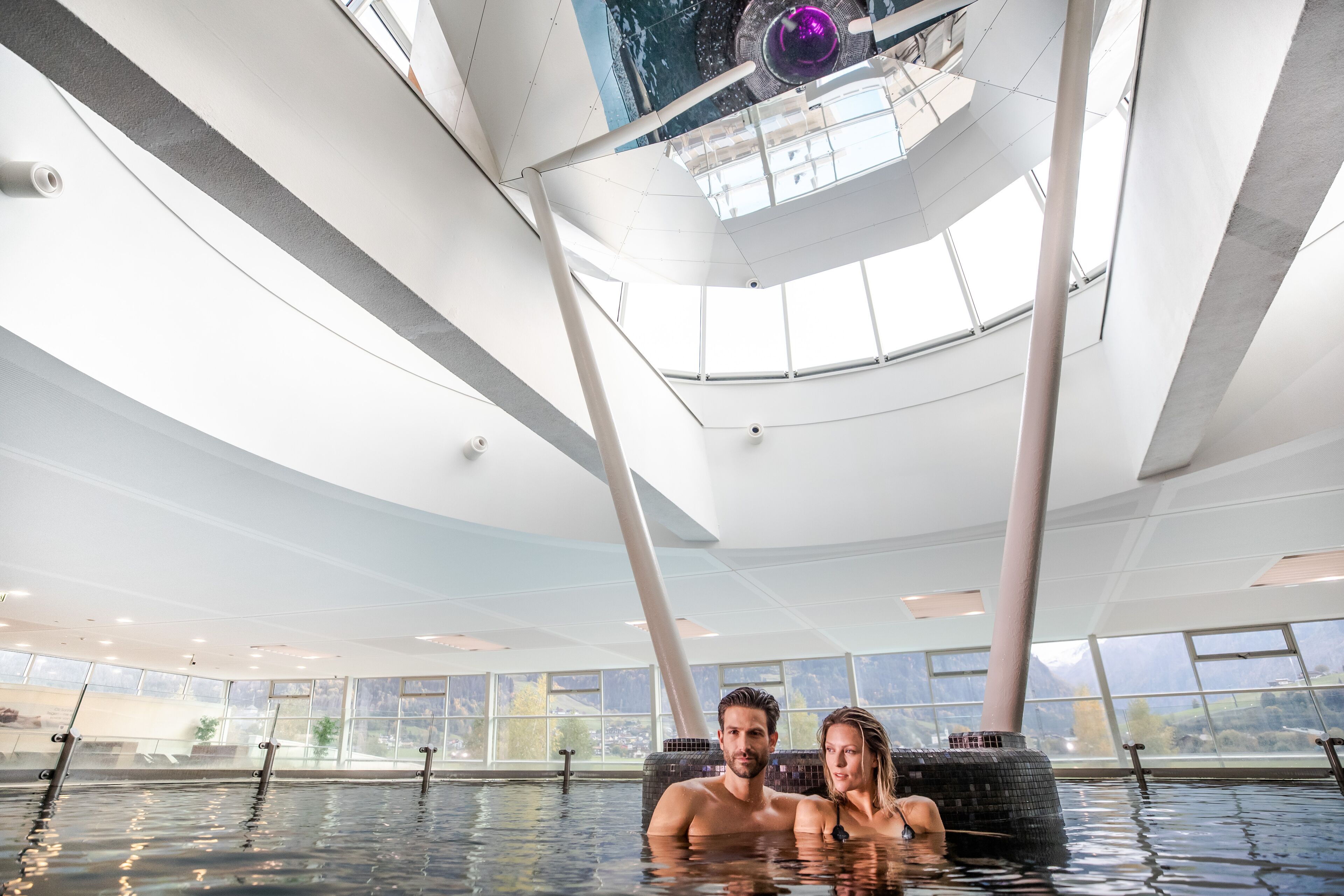 Uma piscina interna ampla com vista desobstruída para o exterior através de grandes janelas.