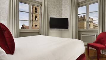 Quarto de hotel com uma cama grande, uma cadeira vermelha e uma televisão fixada na parede.