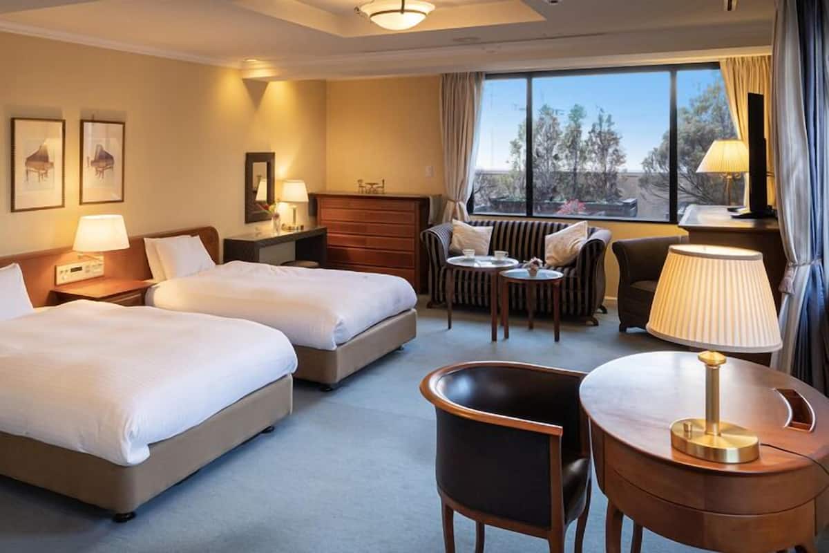 Quarto de hotel com duas camas, um sofá, uma cadeira, uma mesinha e uma janela com vista.