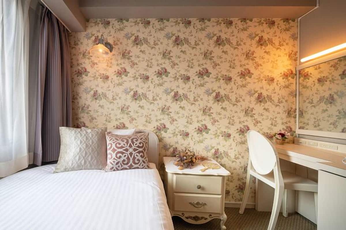 Quarto de hotel com cama, escrivaninha, cadeira, mesa de cabeceira e espelho.