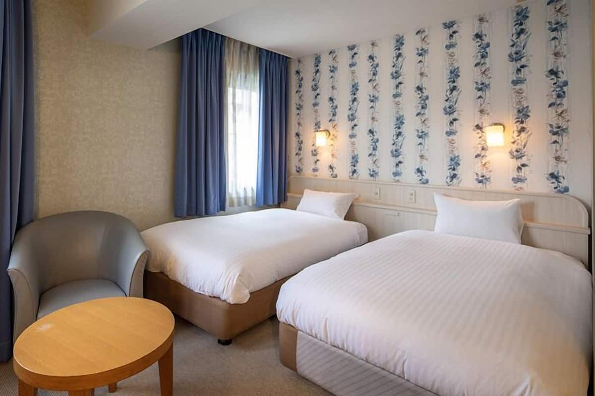 Quarto de hotel com duas camas, uma cadeira e uma pequena mesa.