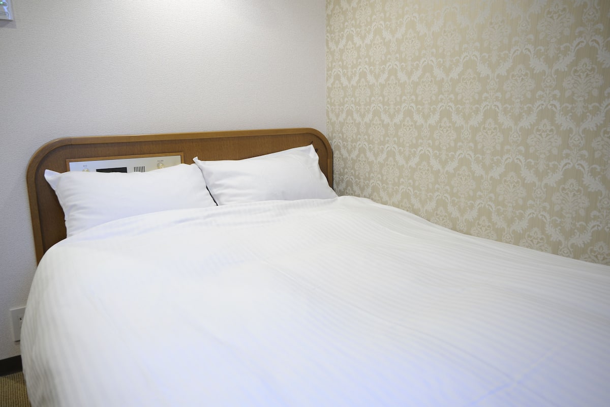 Cama bem arrumada com lençóis brancos e cabeceira de madeira num quarto de hotel com papel de parede estampado.